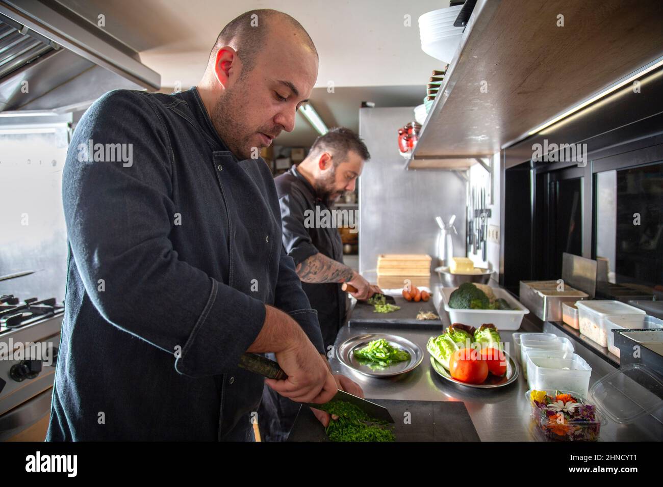 Side view of professional male cooks in uniforms cutting greens and ...