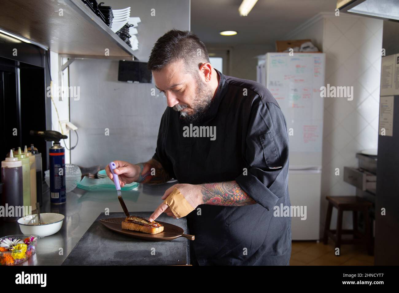 Focused bearded male putting pickled salted fish on toast served on ...