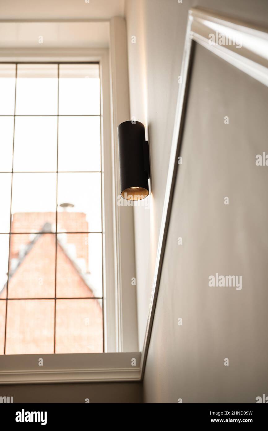 From below of stylish black lamp hanging on gray wall near big glass ...
