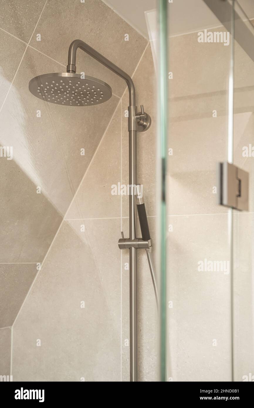Metallic shower head hanging on tiled wall in bathroom of modern ...