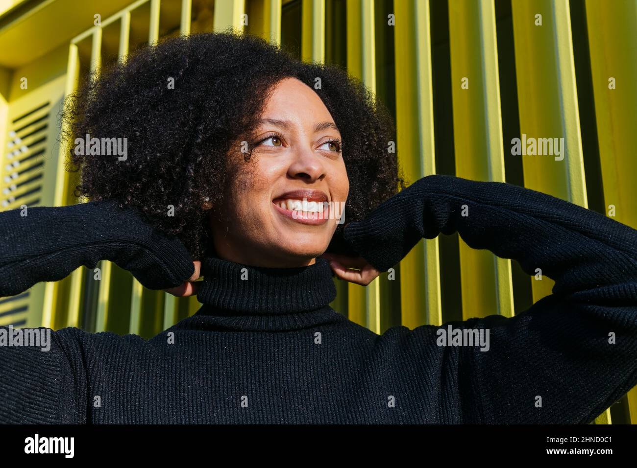 Delighted African American female in black turtleneck touching hair and ...