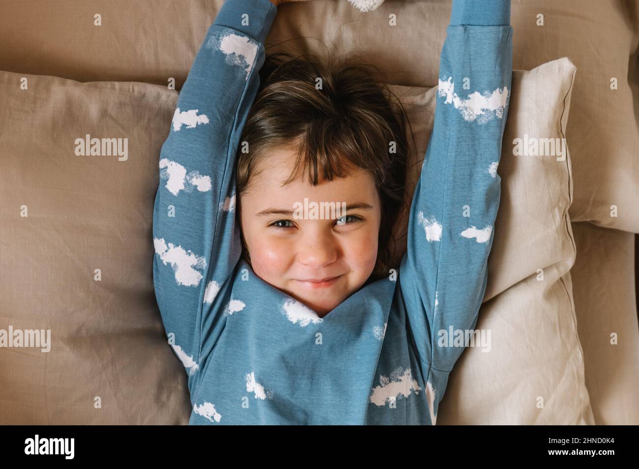 Top view of smiling girl in sleepwear looking at camera while lying on ...