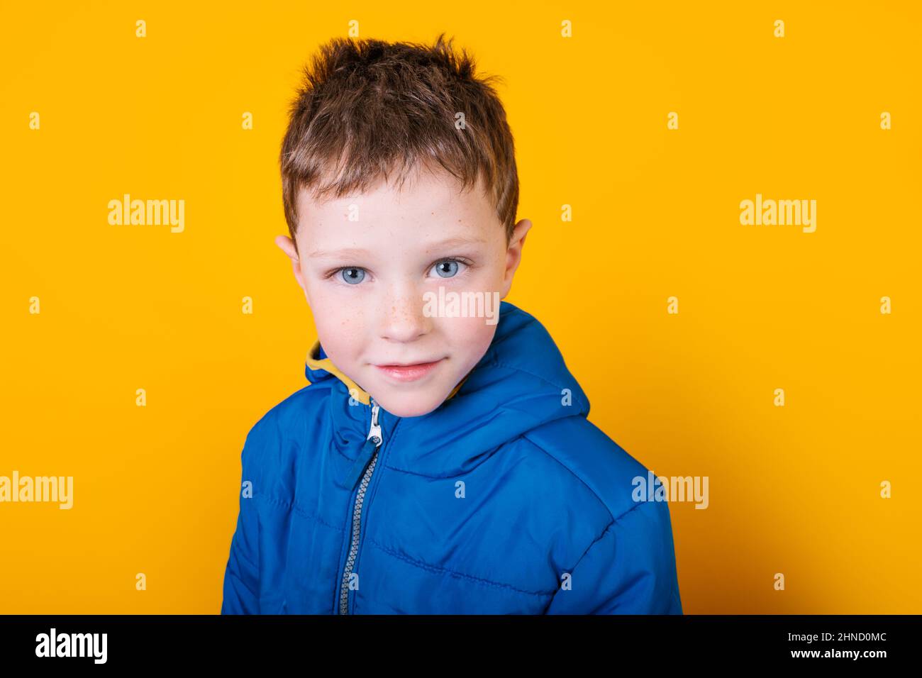 Cute boy in warm bright coat with blue eyes looking at camera against ...
