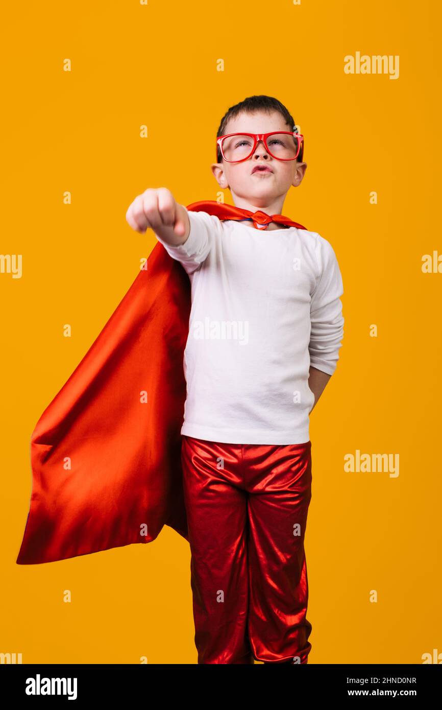 Child in red superhero clothes and eyeglasses stretching arm while ...