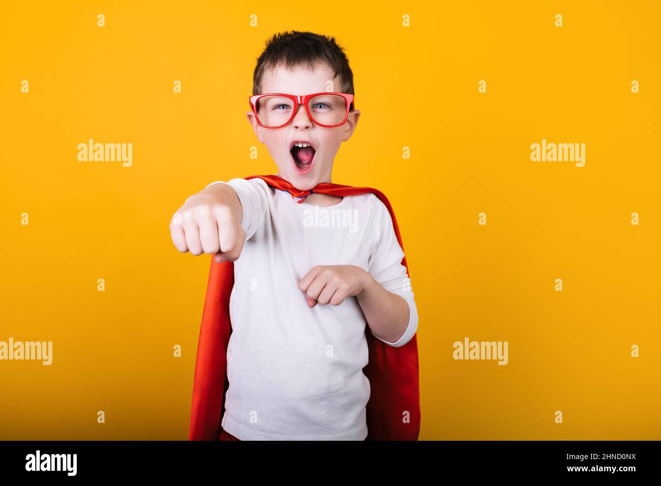 Child in red superhero clothes and eyeglasses stretching arm while ...
