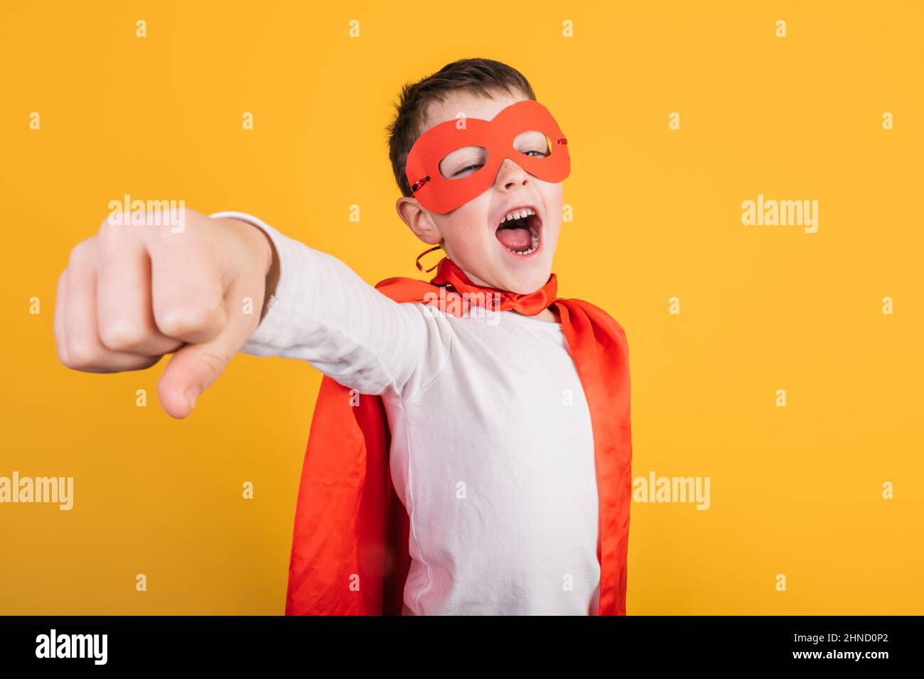 Child in red superhero clothes and mask stretching arm while standing ...