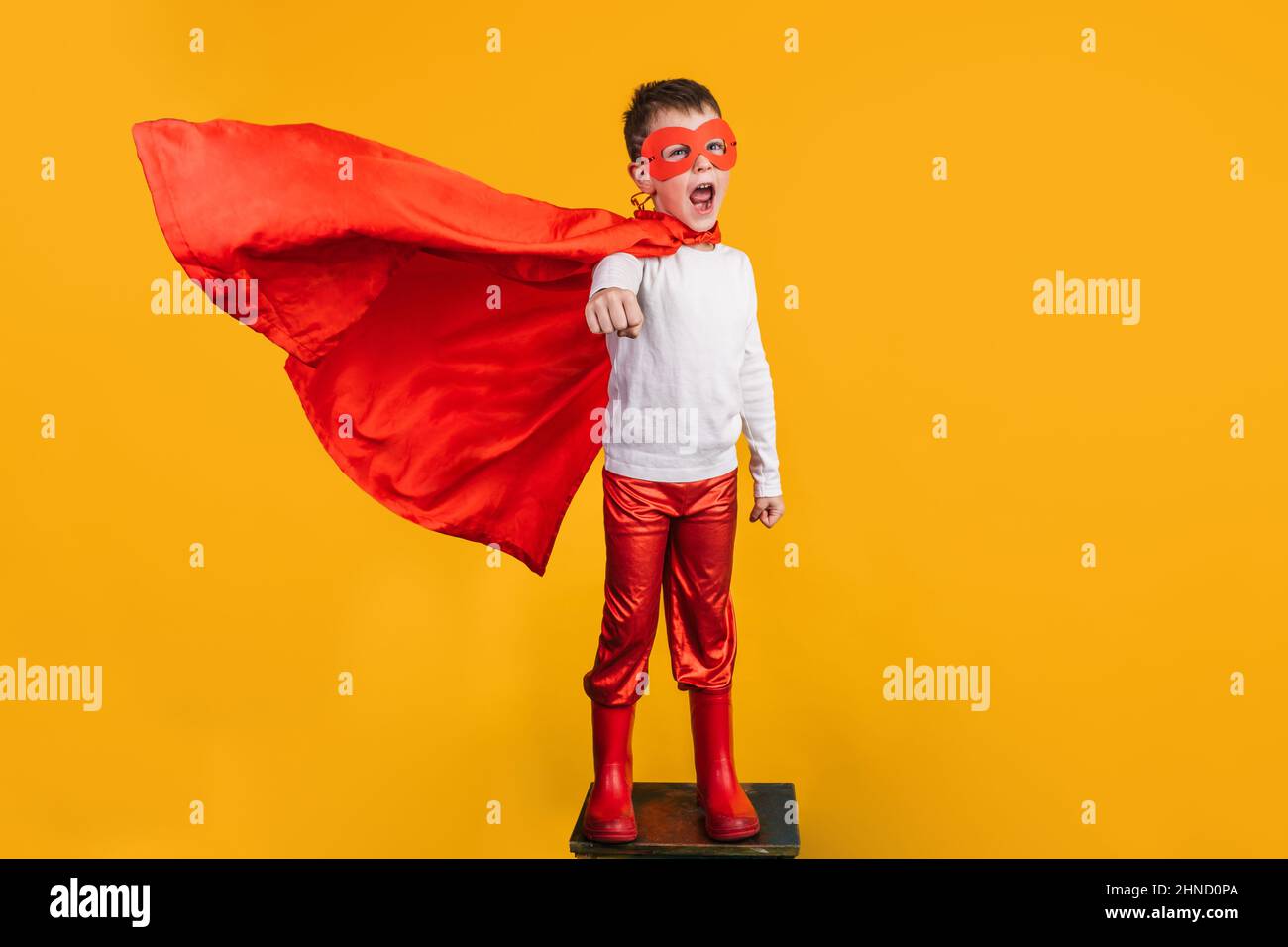 Child in red superhero clothes and mask stretching arm while standing ...