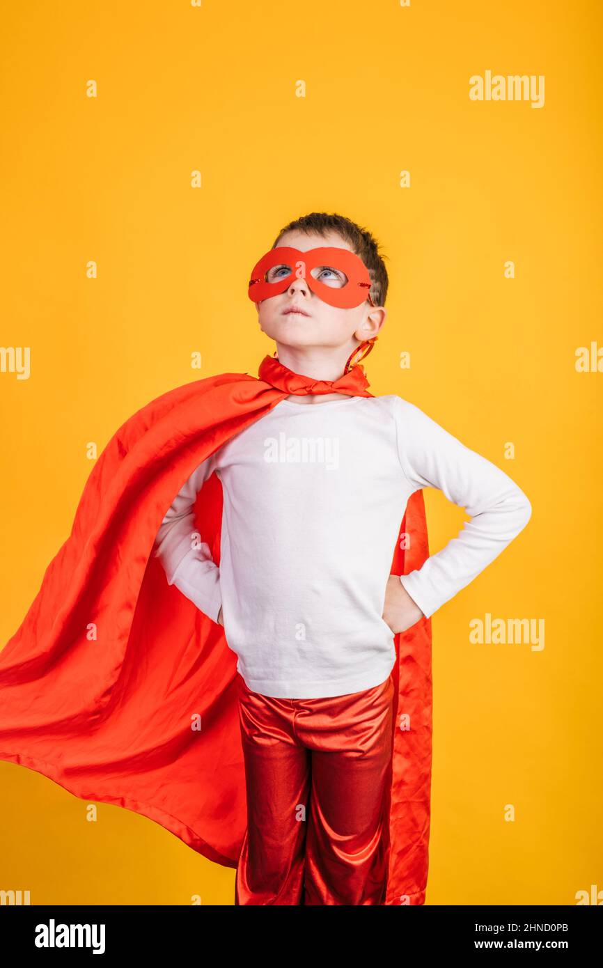 Brave kid in red superhero cape and mask looking up dreamily while ...