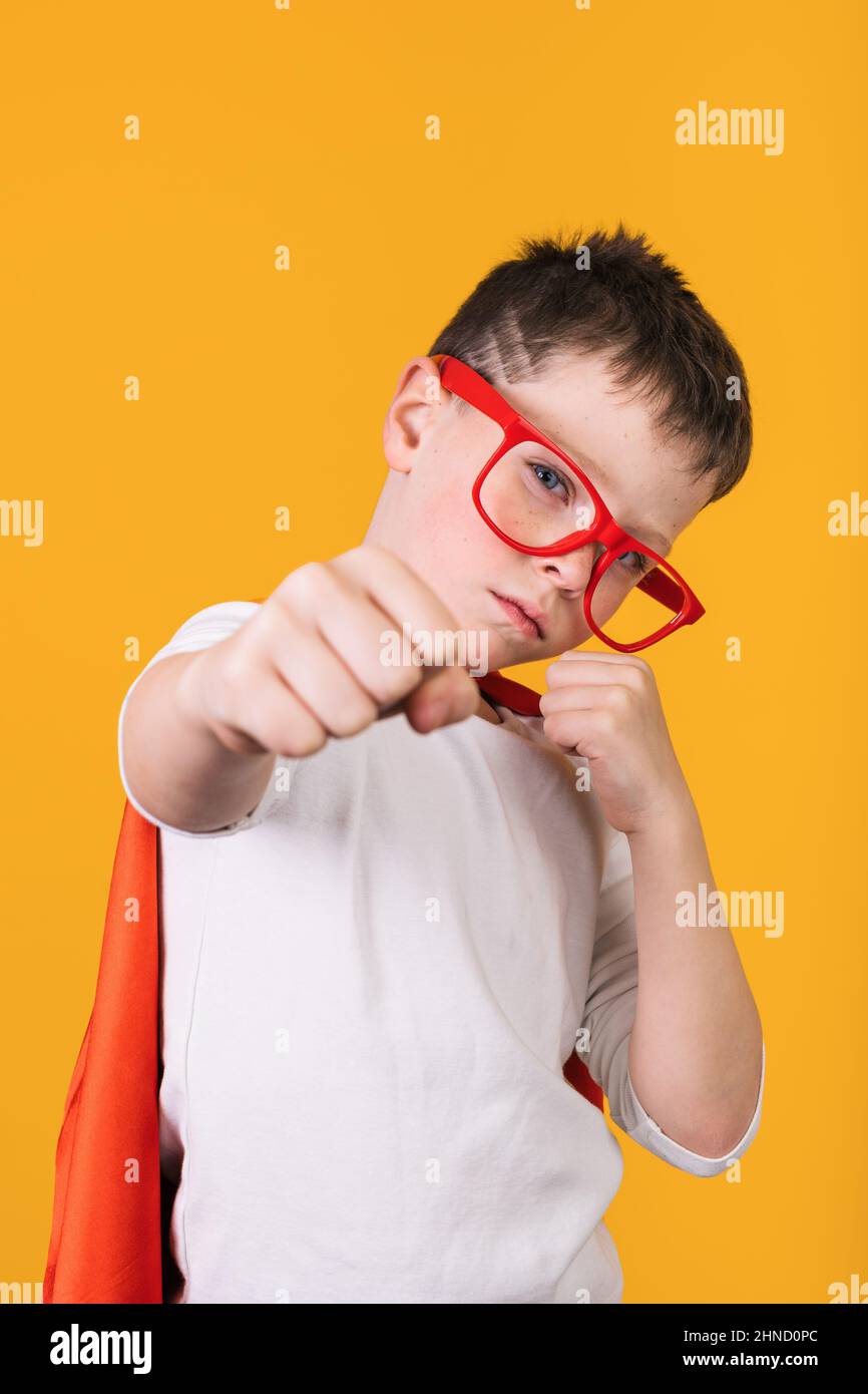 Child in red superhero clothes and eyeglasses stretching arm while ...
