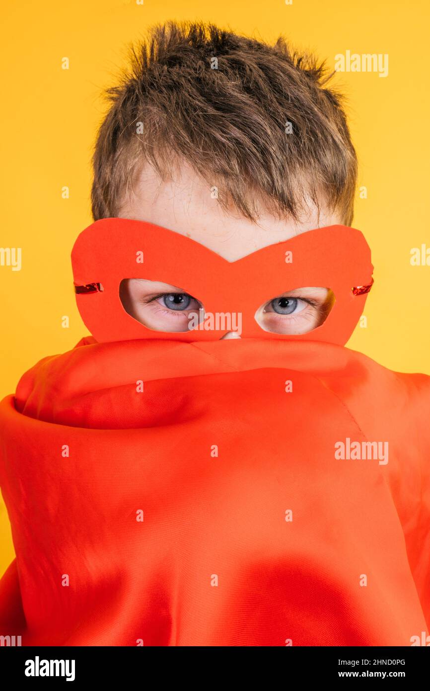 Little child wearing superhero mask and hiding face behind red cloak ...