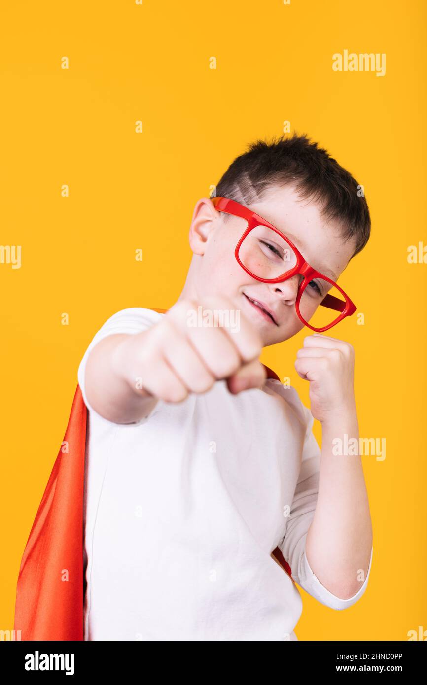 Child in red superhero clothes and eyeglasses stretching arm while ...