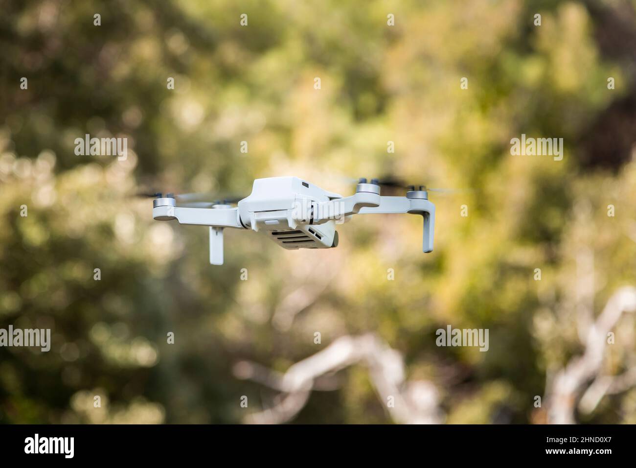 Soft focus of modern white unmanned drone flying in air near high green ...