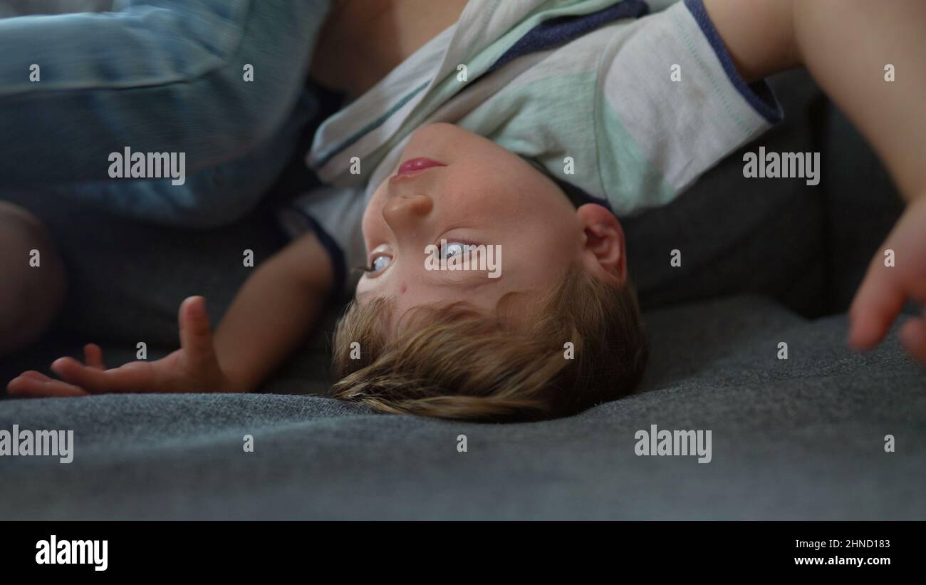 Bored little boy at home in upside down on sofa child playing alone ...