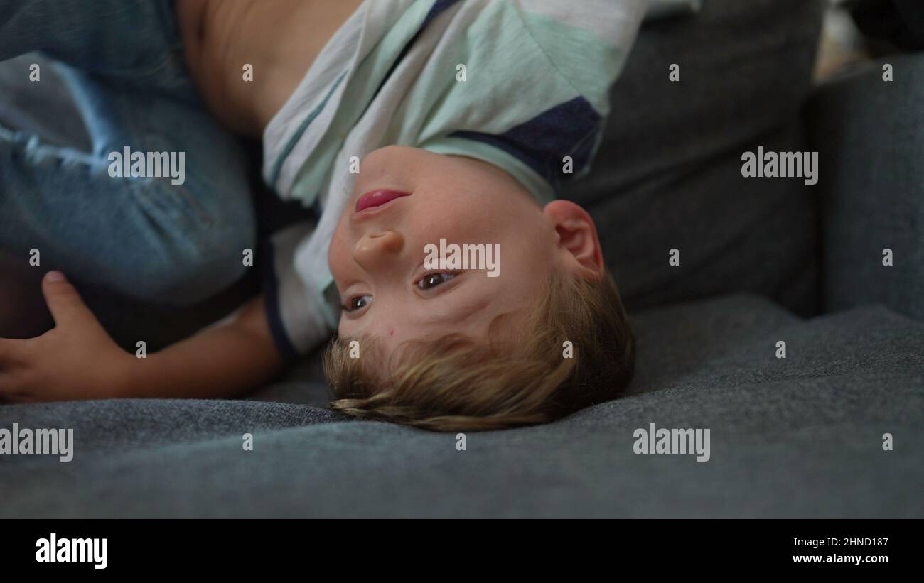 Bored little boy at home in upside down on sofa child playing alone ...