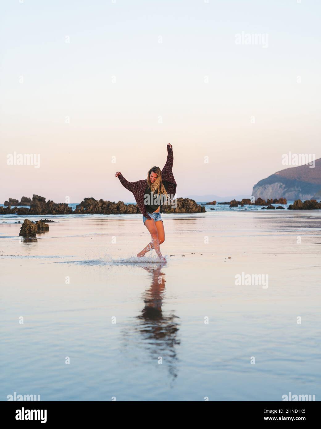 Full body of positive fit female making dancing move on wet coast near ...