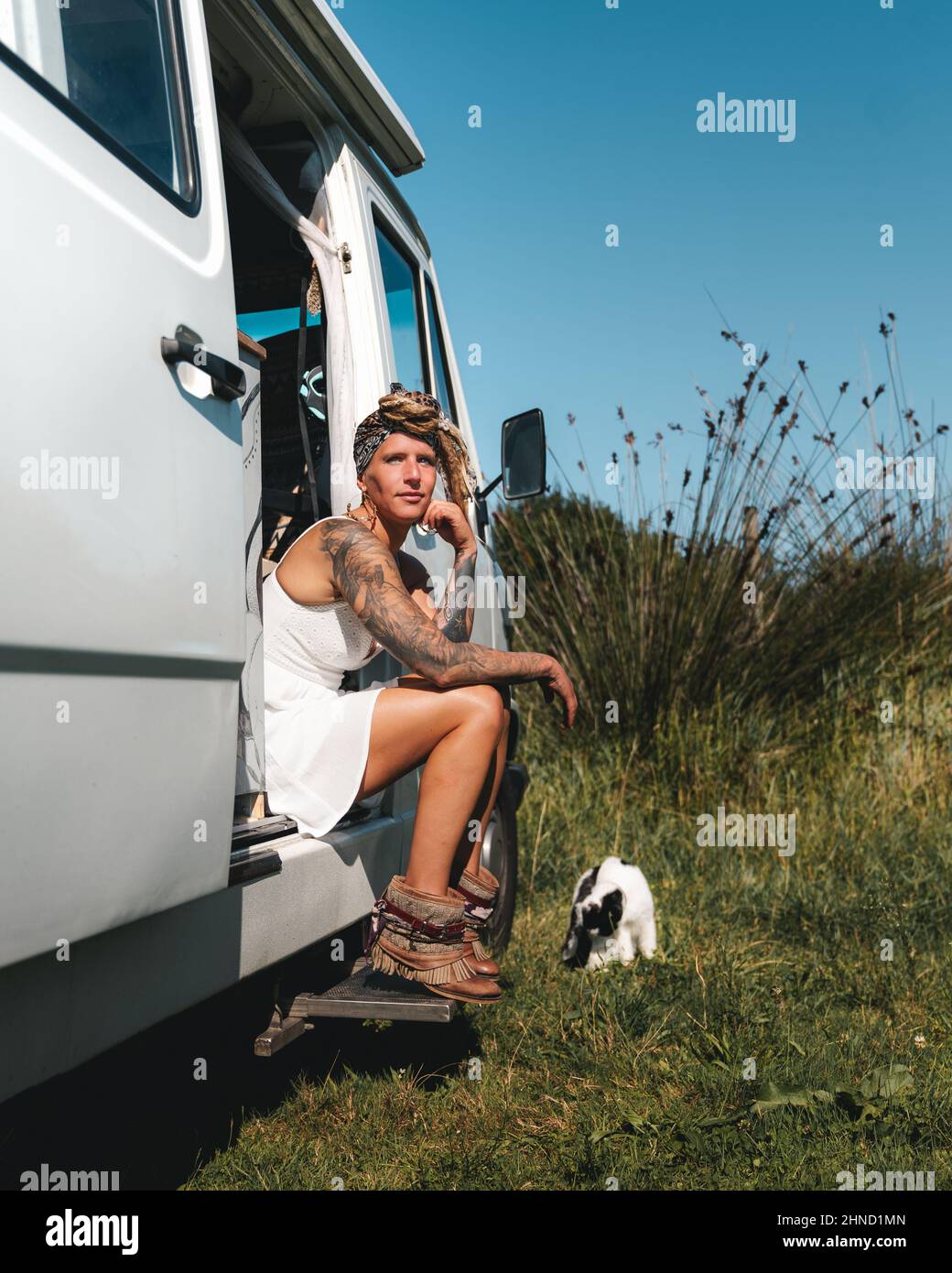 Side view of female traveler with dreadlocks sitting in camp van with ...