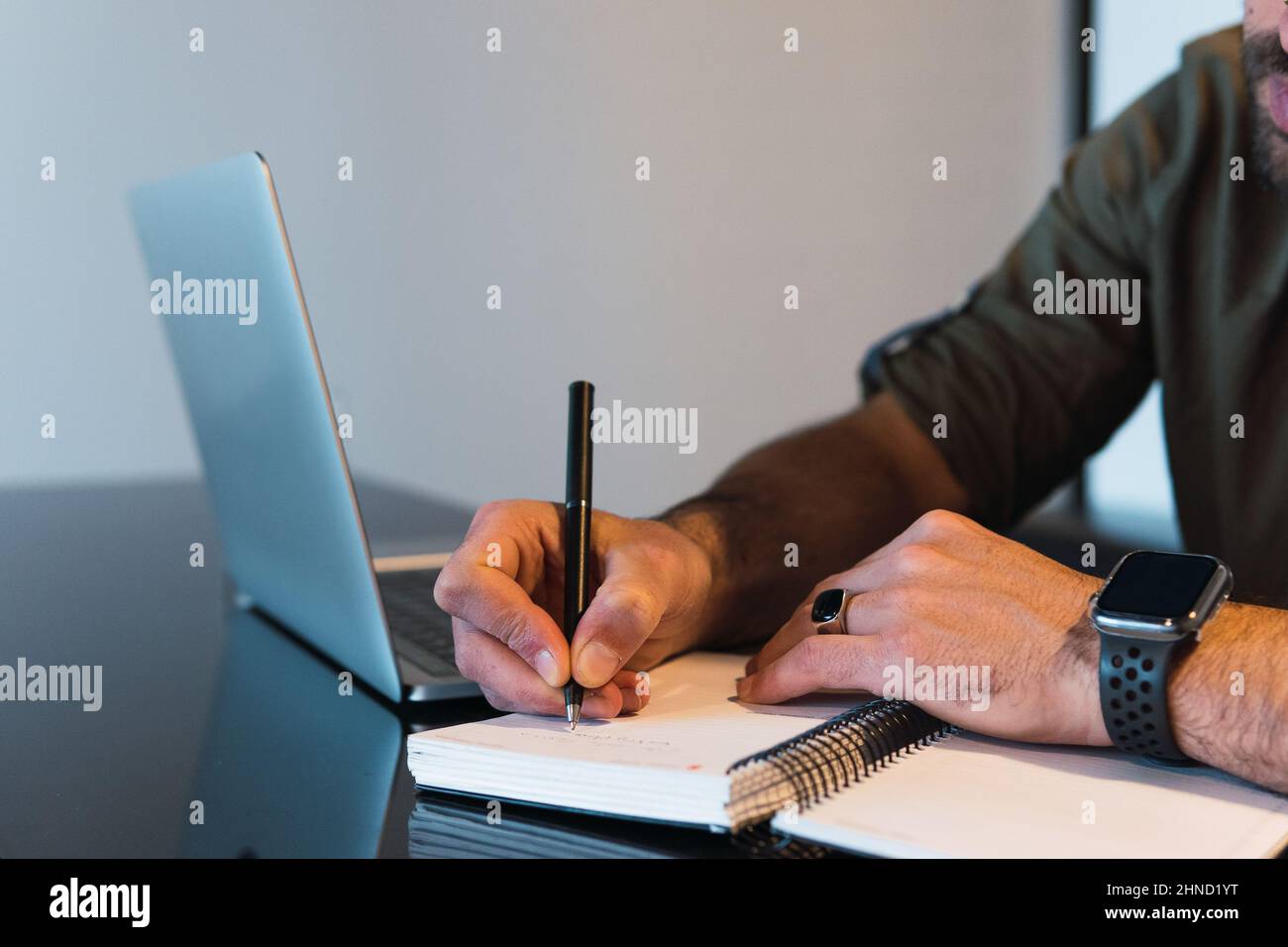 Crop unrecognizable male taking notes in notepad while sitting at table ...