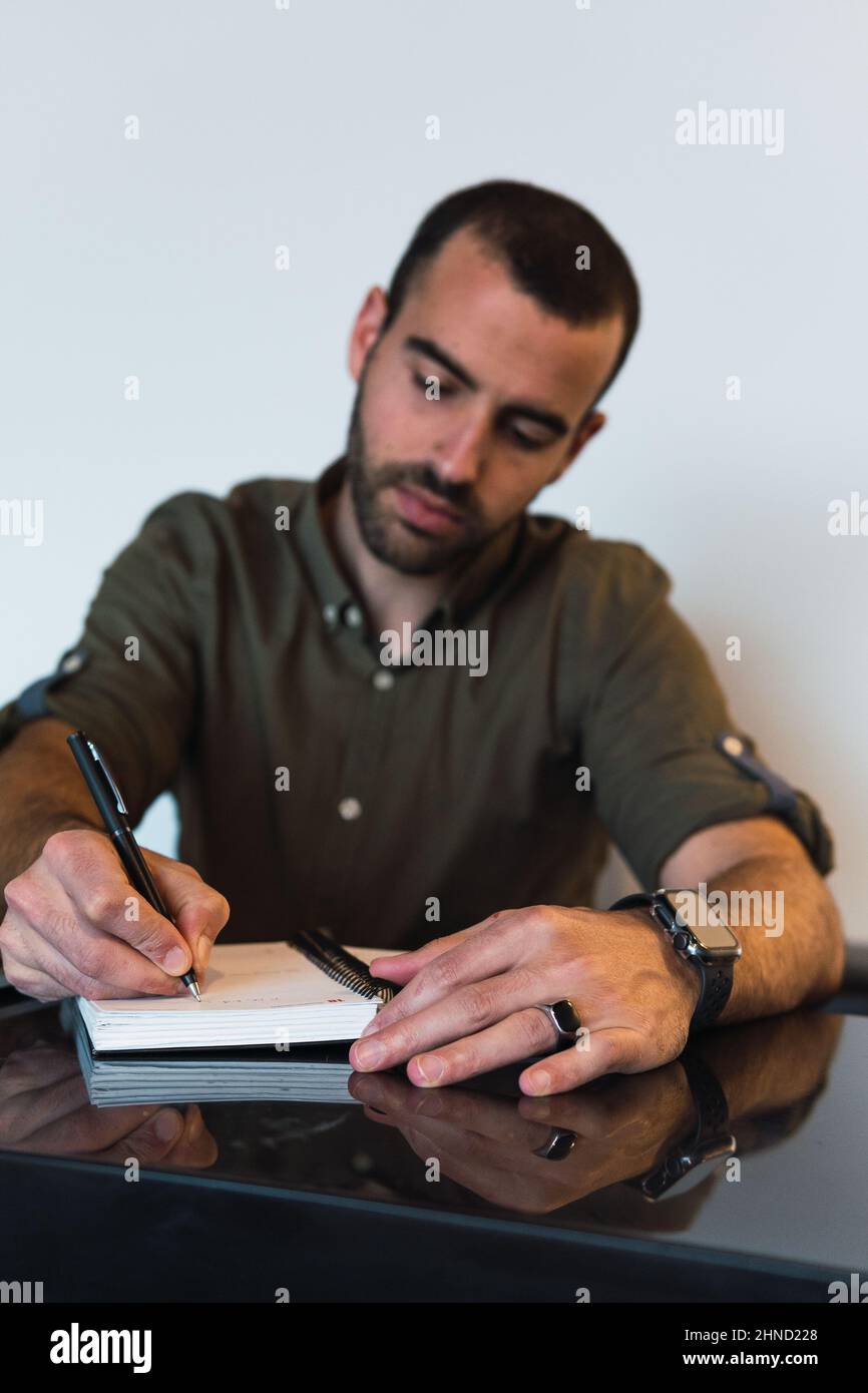 Focused male taking notes in notepad while sitting at table in light ...