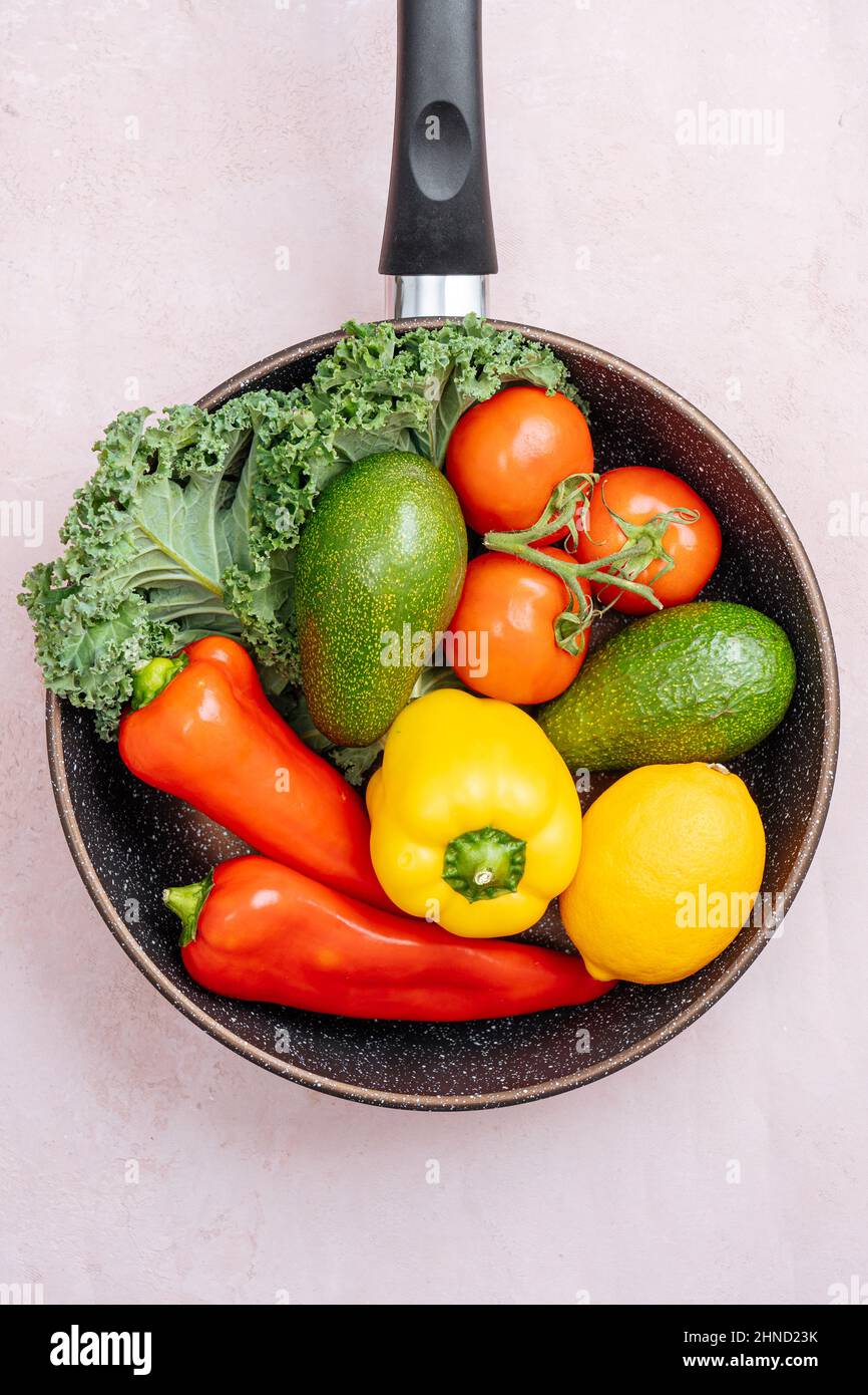 Top view of frying pan with raw ripe peppers and avocados near cherry ...