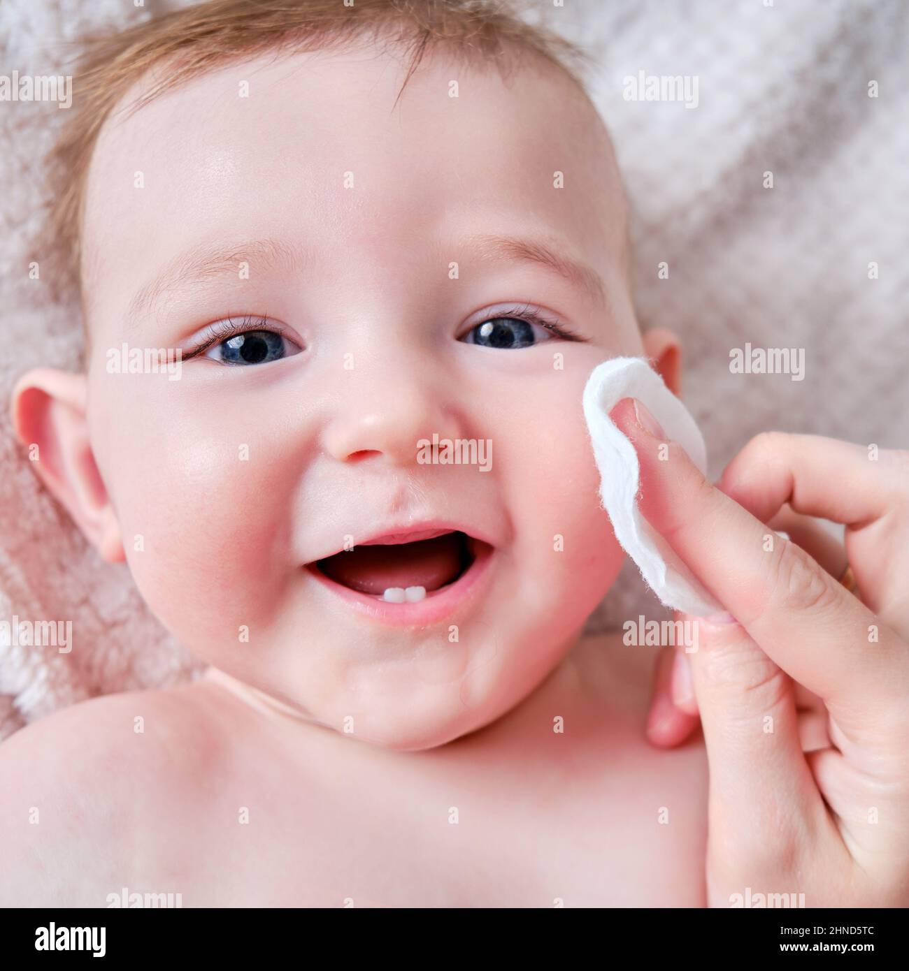 Mother hands wash the face of a happy infant baby with a cotton pad ...