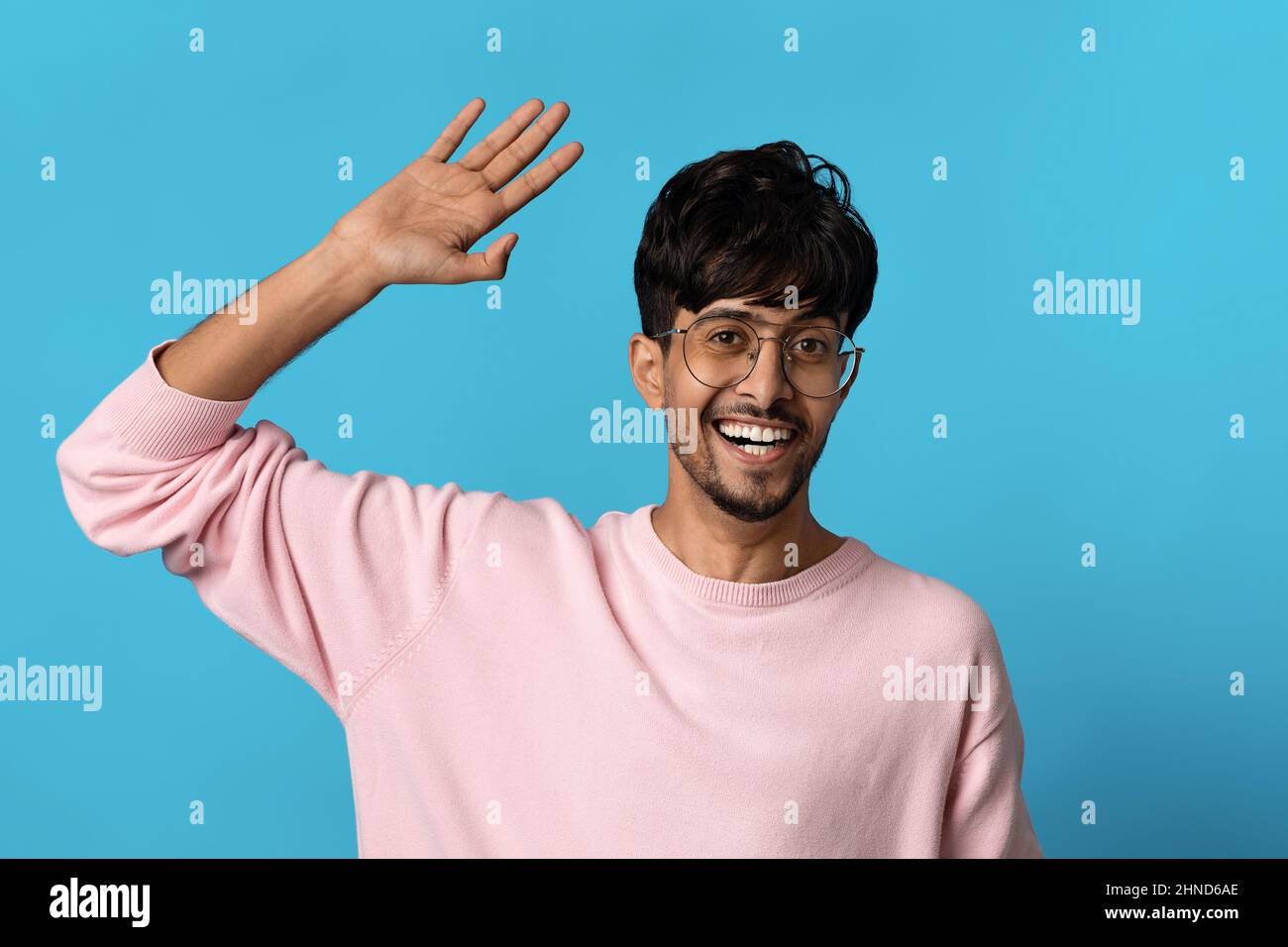 Positive middle eastern guy waving at camera on blue Stock Photo - Alamy