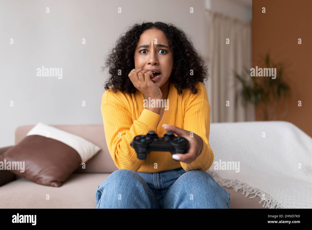 Terrified young African American woman sitting on couch with joystick ...