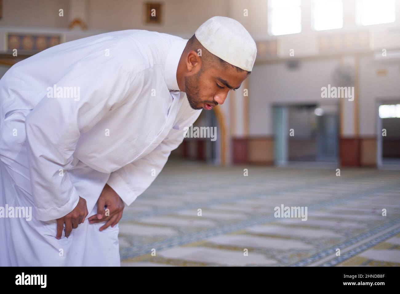 A side close view of a young Muslim man bowing during prayers at a ...