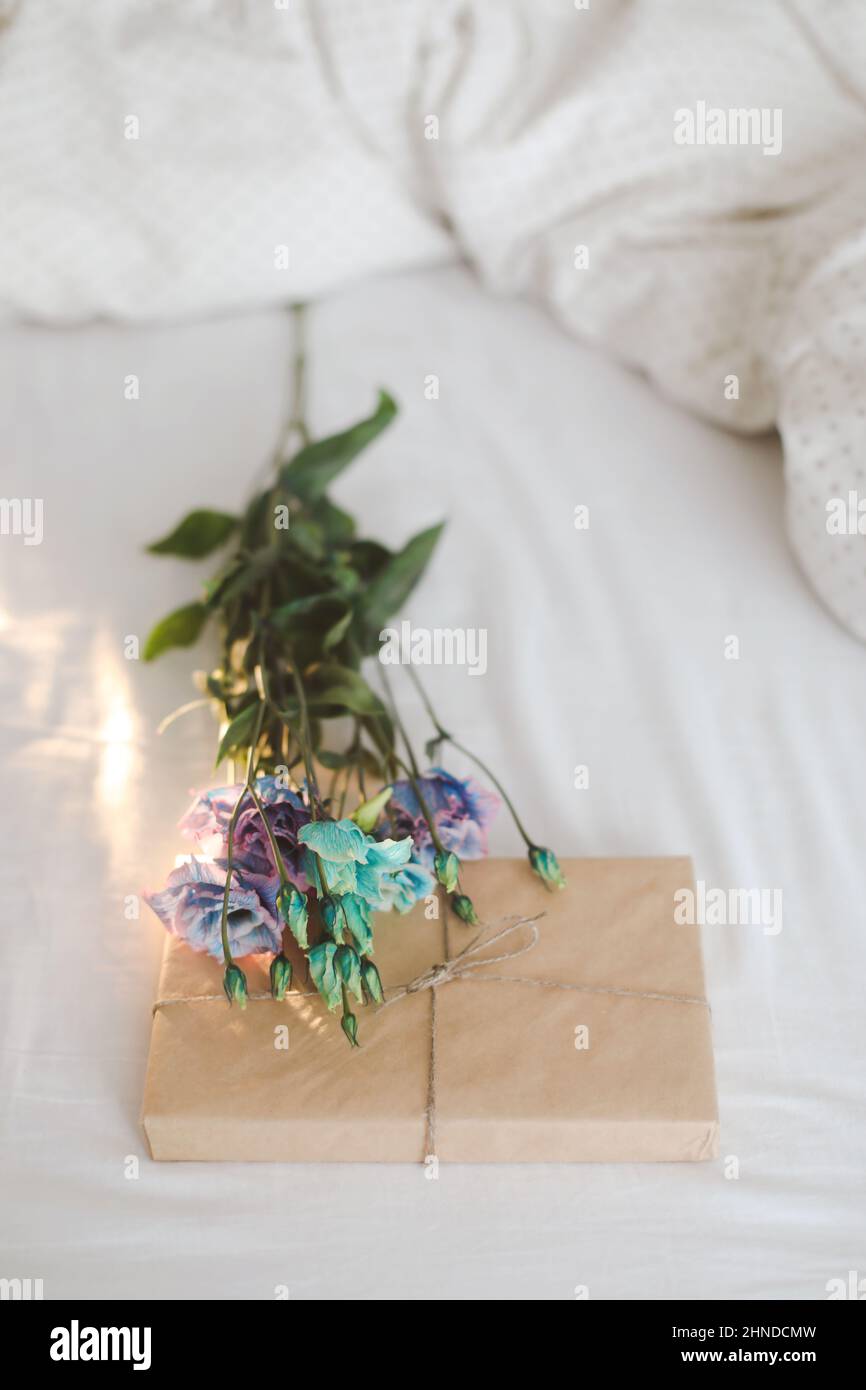 Bouquet of flowers and a gift covered in paper on crumpled white bed ...