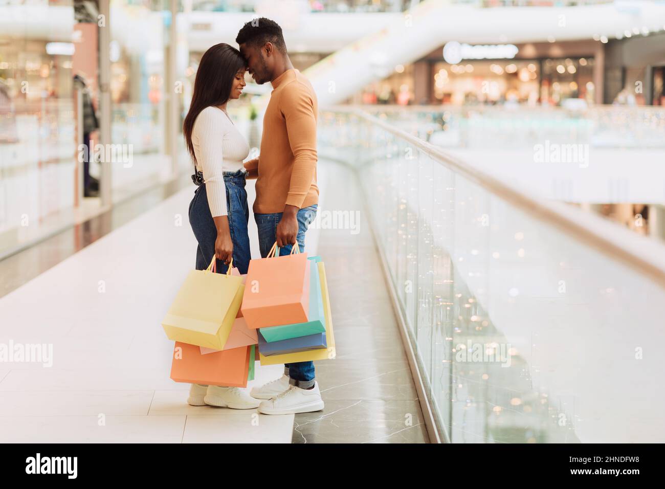 Cheerful young black couple hugging and holding shopping bags Stock ...