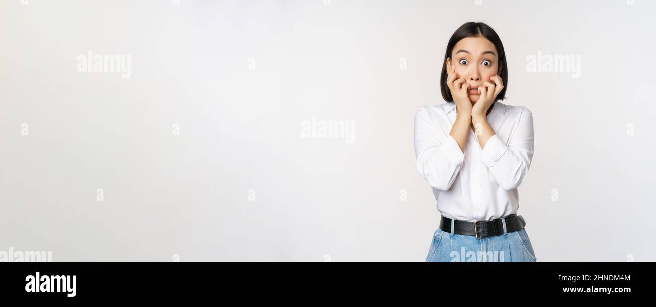 Portrait of scared asian woman watching smth scary, biting fingers on ...