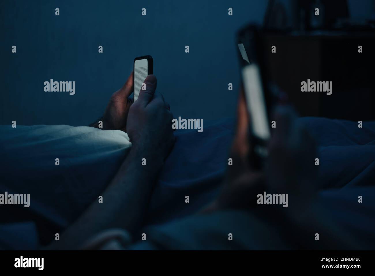 A man and a woman lie in pastels at night and use their phones ...