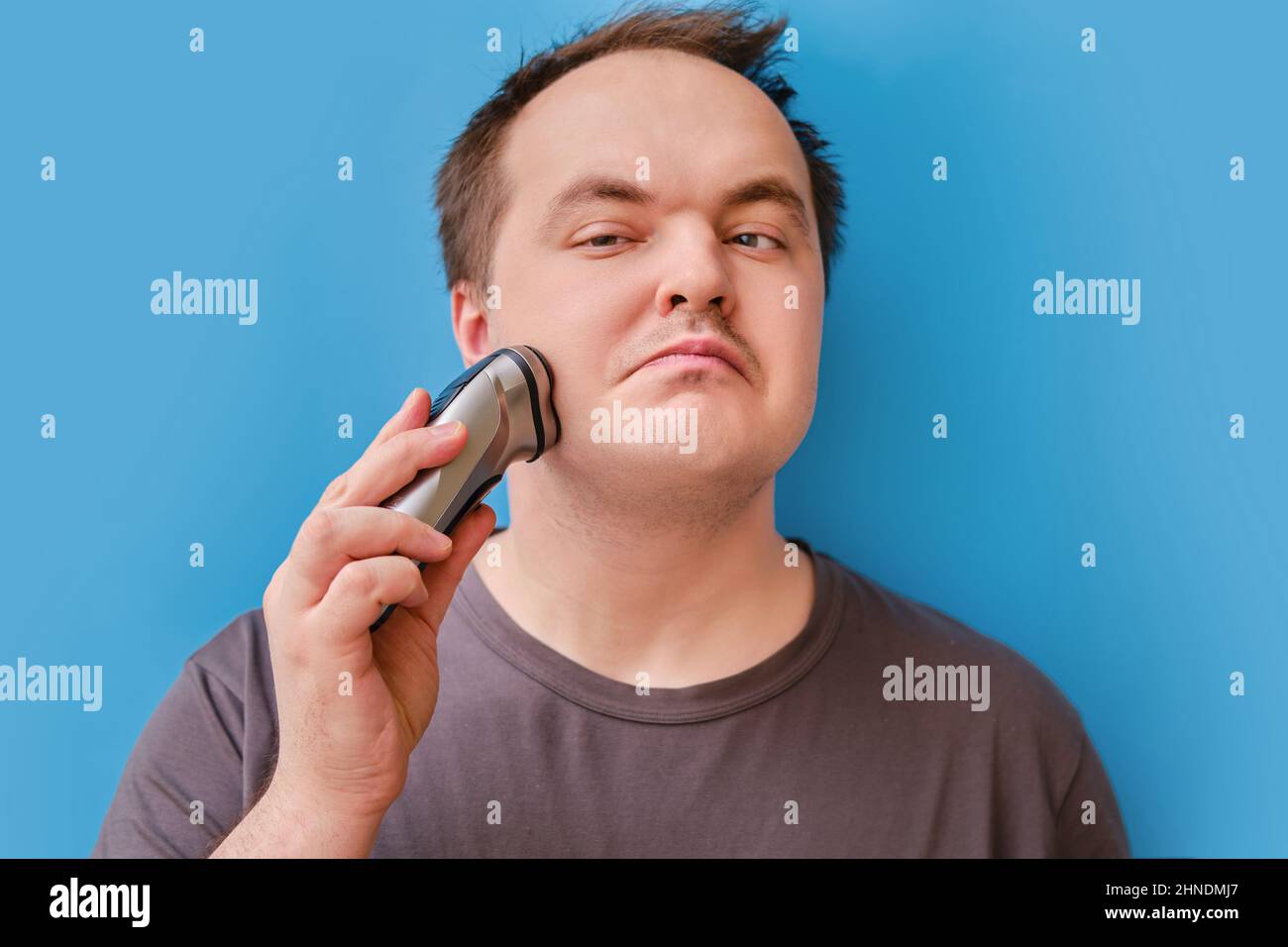 Portrait of disheveled adult man shaving stubble with electric razor ...