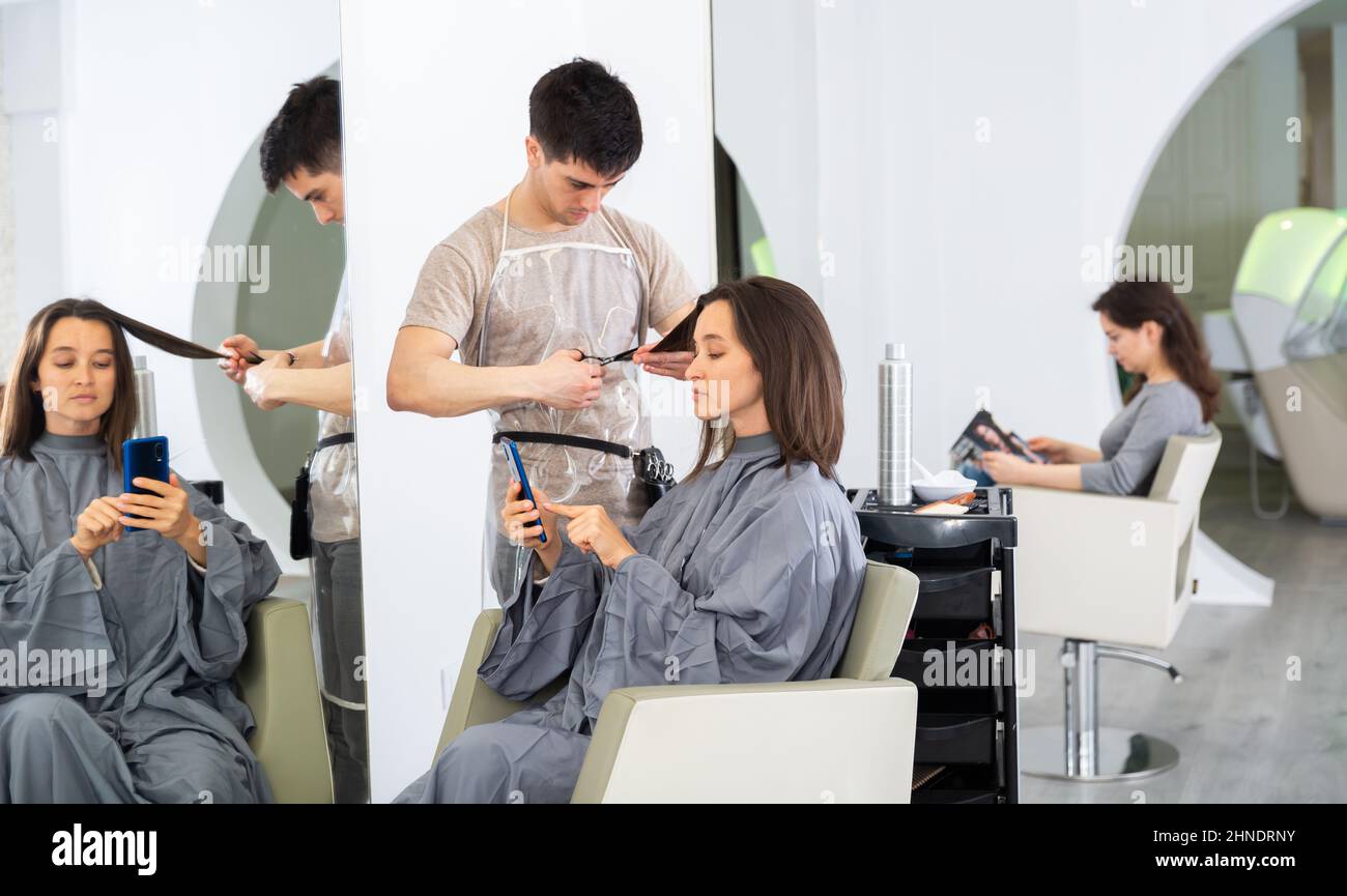 Girl client using phone during hair cut by professional hairdresser ...