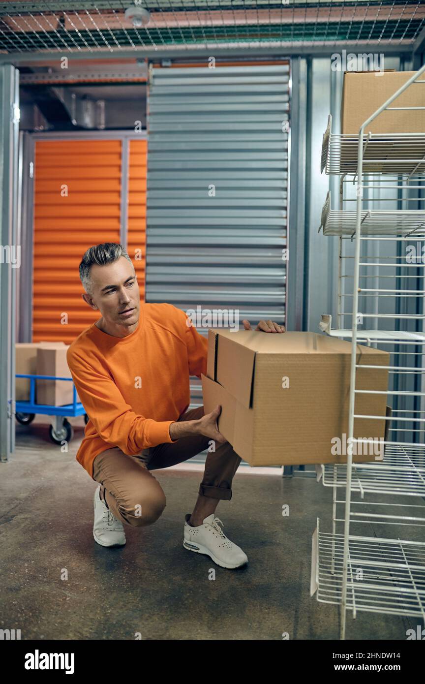 Concentrated storehouse employee placing boxed goods on the shelving ...