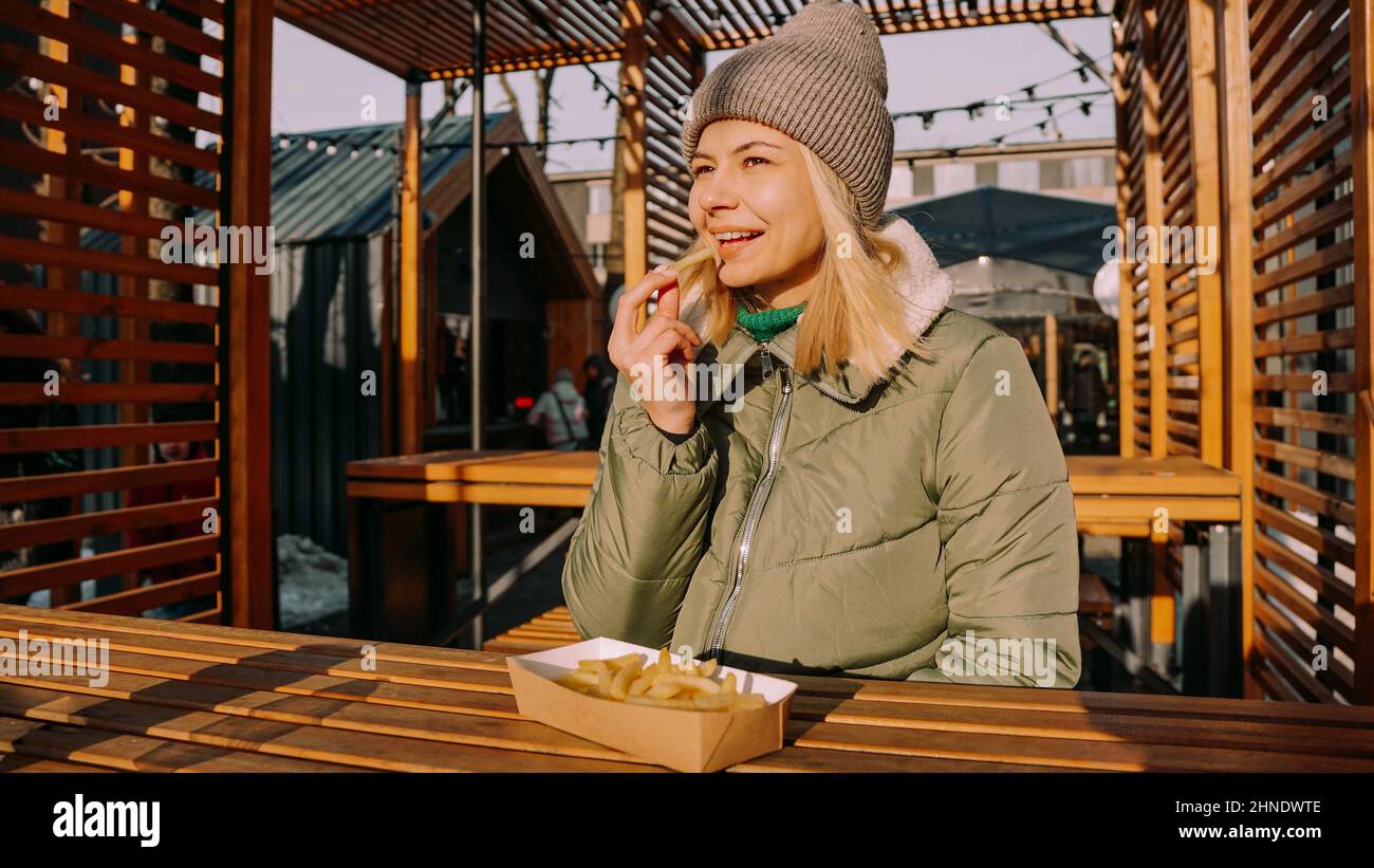 Woman eating tasty french fries in outdoor cafe. Sunny winter day ...