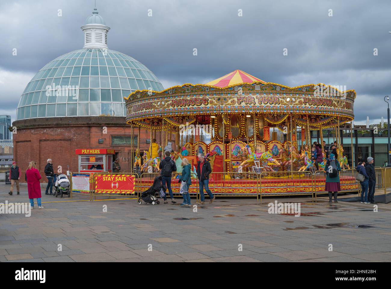 People out and about in Greenwich enjoy a funfair carousel ride. Domed ...