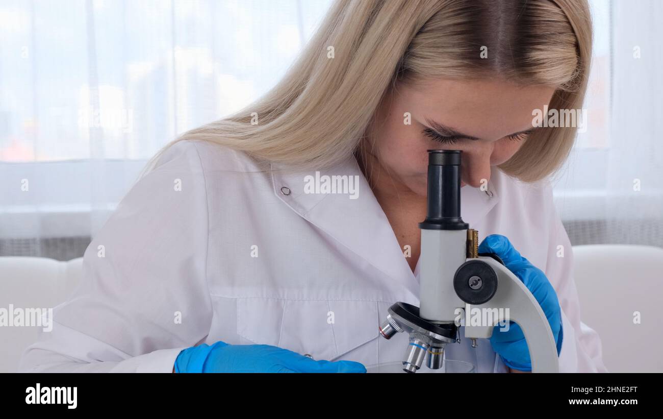 Female laboratory assistant analyzes samples using a microscope while ...