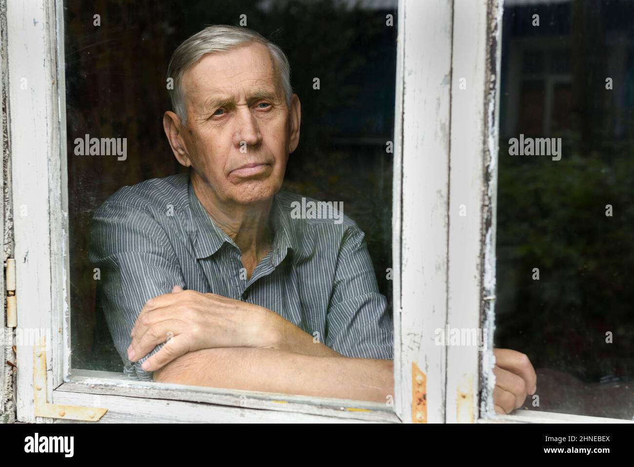 Portrait through the glass window. A sad elderly man of 80 years old ...