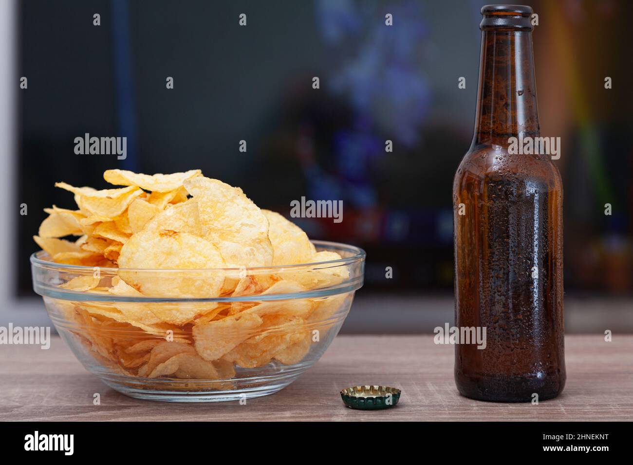 A clear glass bowl full of chips, a bottle of fresh beer and a bottle ...