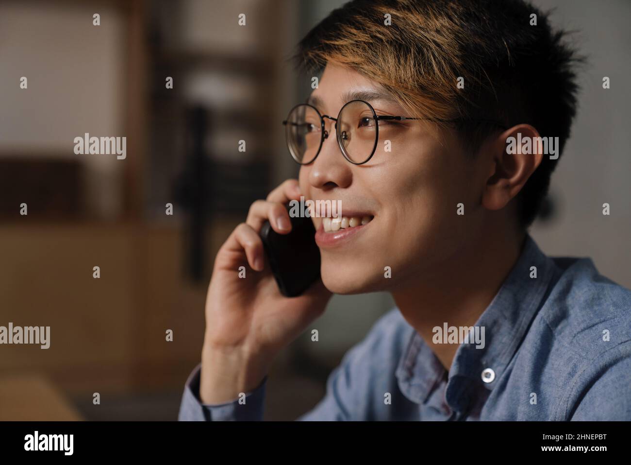 Happy asian guy in eyeglasses talking on mobile phone while working in ...