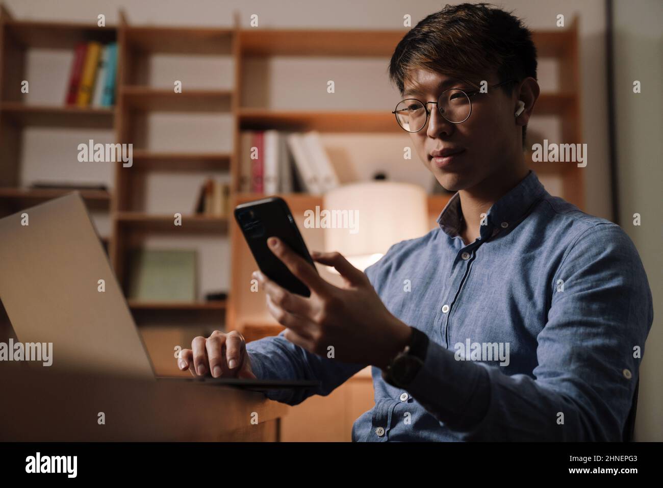 Focused asian guy in earphones using mobile phone while working with ...