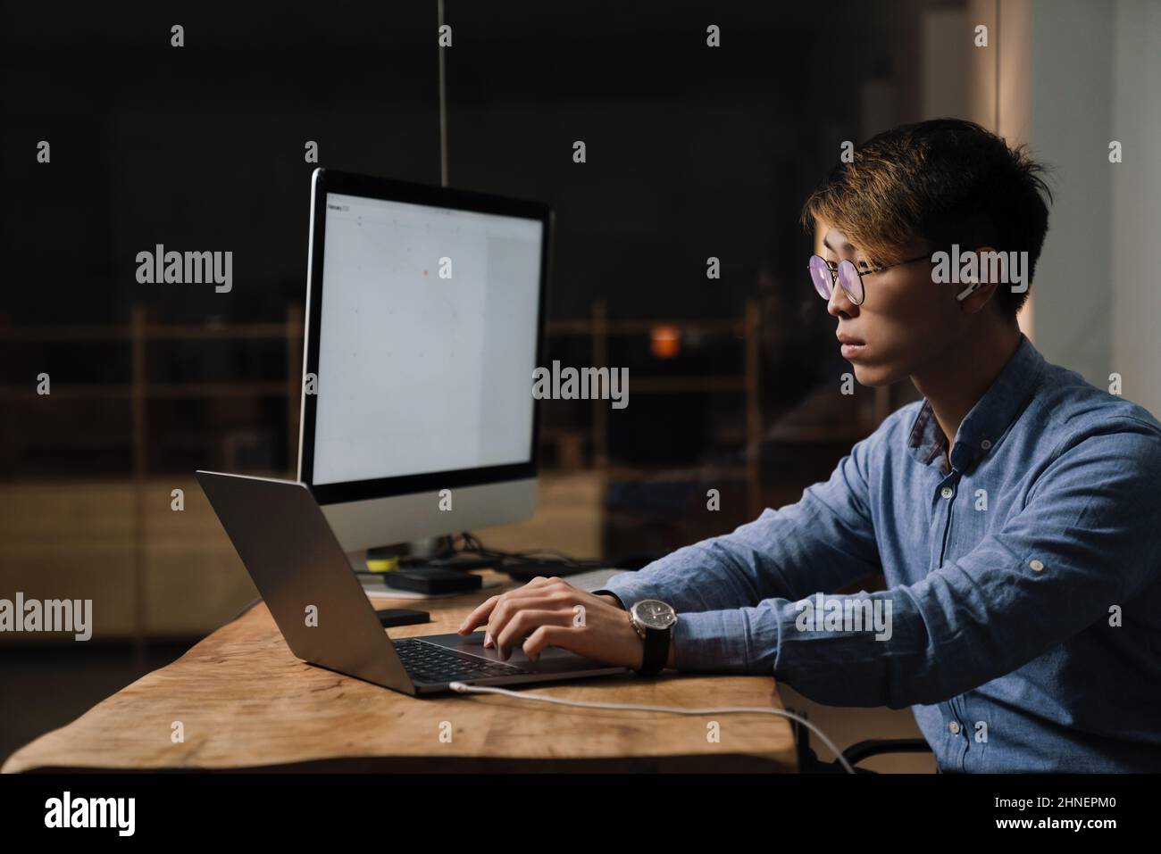 Focused asian guy in earphones working with laptop and computer in ...