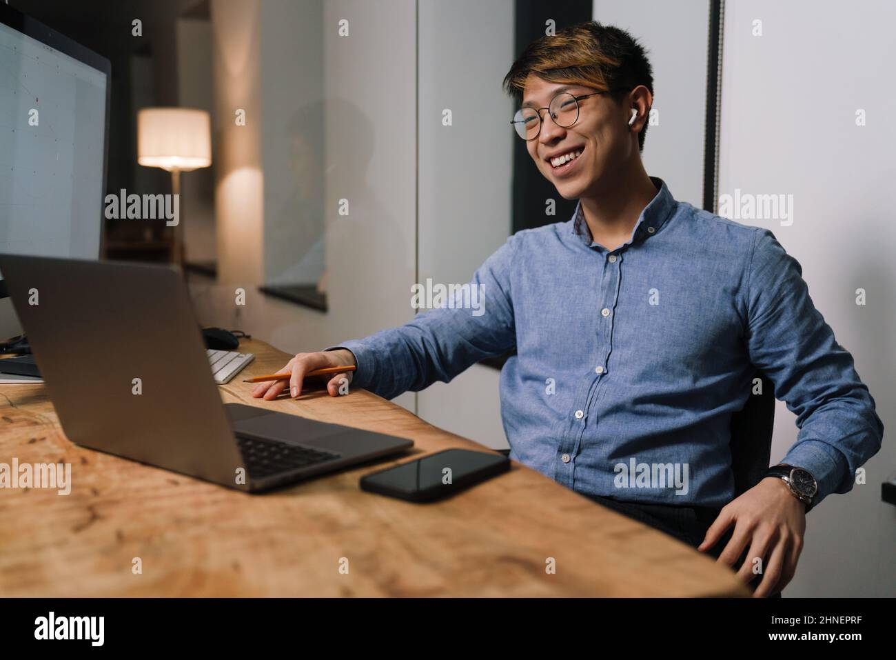 Happy asian guy in earphones smiling while working with laptop in ...