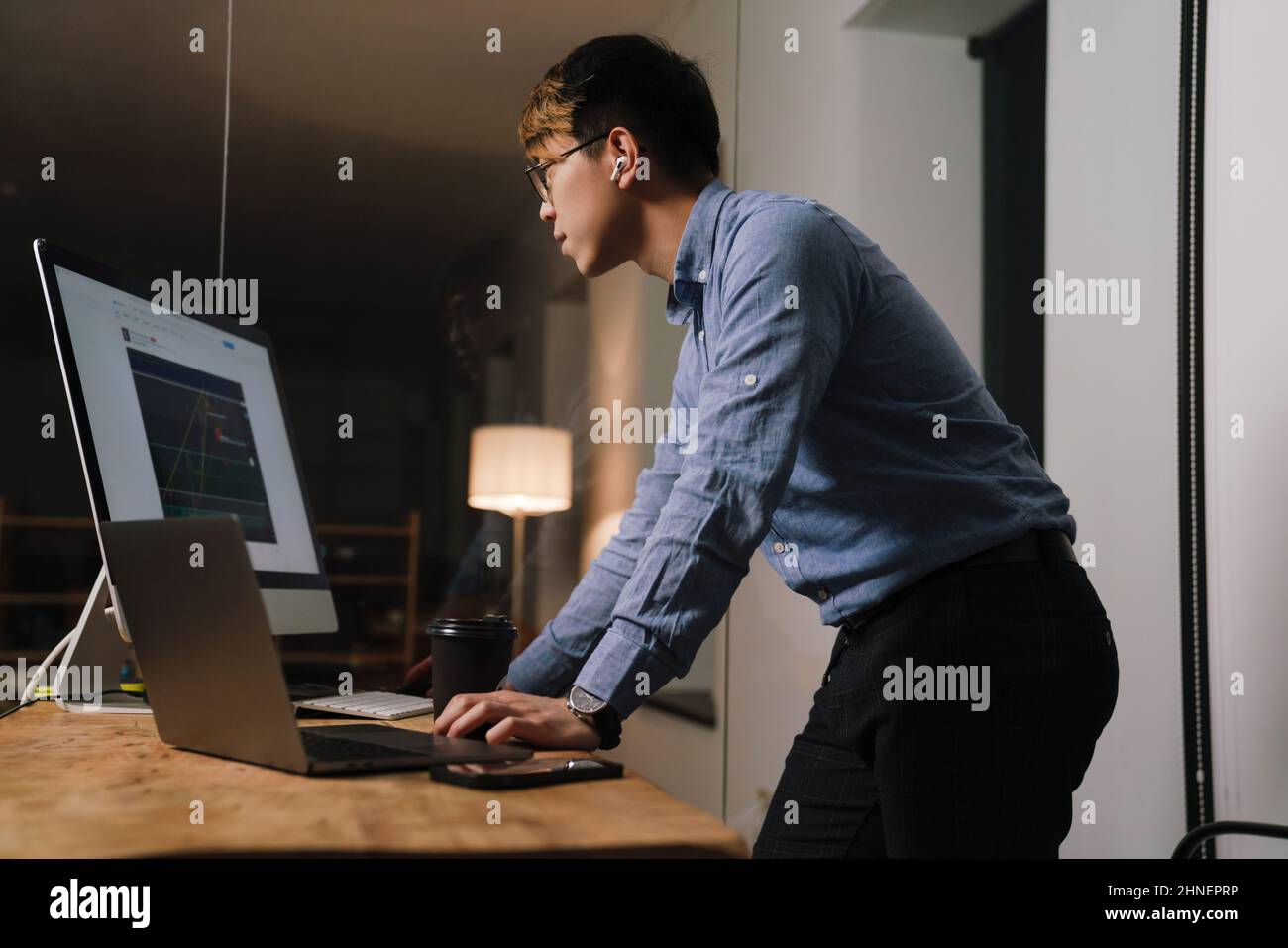 Focused asian guy in earphones working with laptop and computer at ...