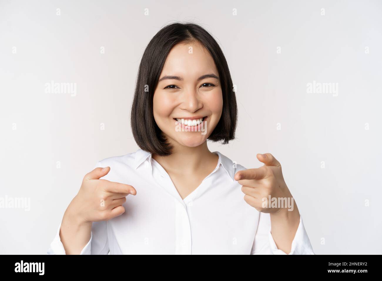 Close up of enthusiastic young woman smiling, pointing fingers at ...