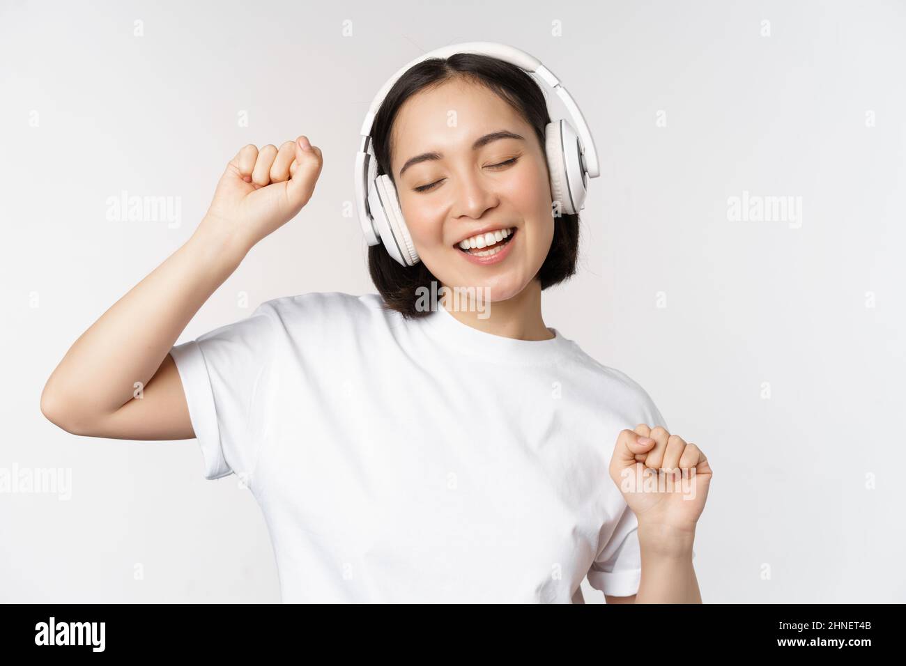 Dancing and singing asian woman, listening music in headphones ...