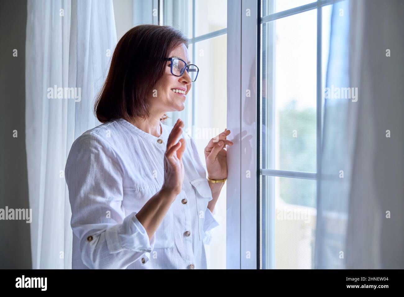 Mature woman waving hand looking out the window, seeing off, greeting ...