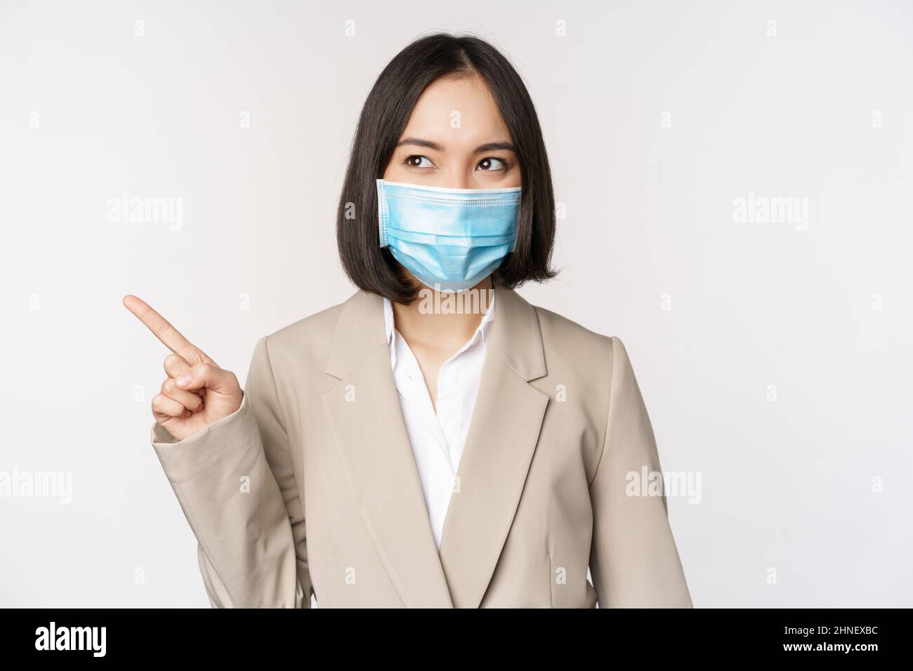 Enthusiastic businesswoman pointing fingers left, wearing medical face ...