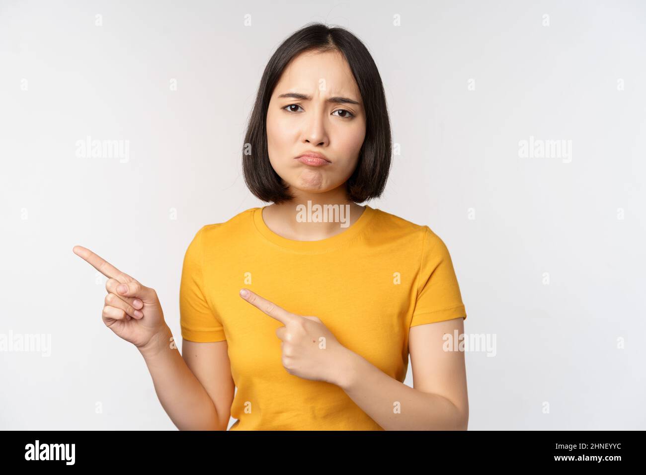 Portrait of disappointed brunette asian girl, pointing fingers left ...
