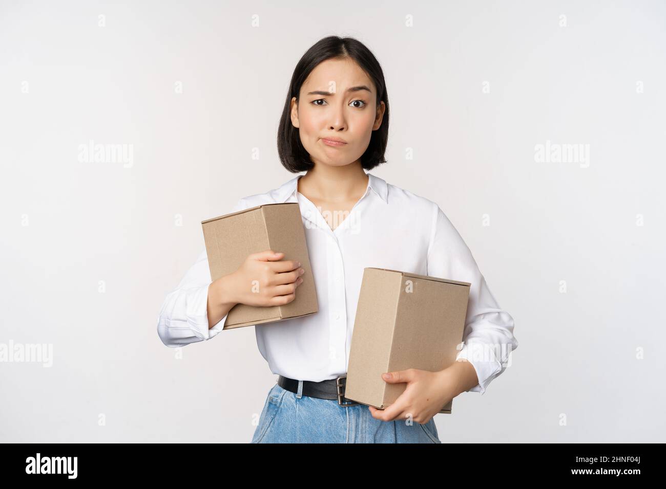 Complicated young asian woman holding two boxes, looking doubtful at ...